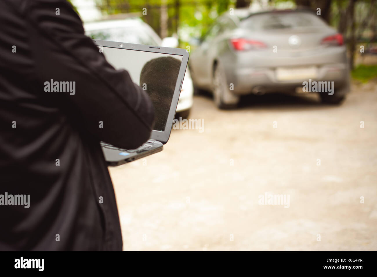man with a laptop in parking lot in yard near car is doing ...