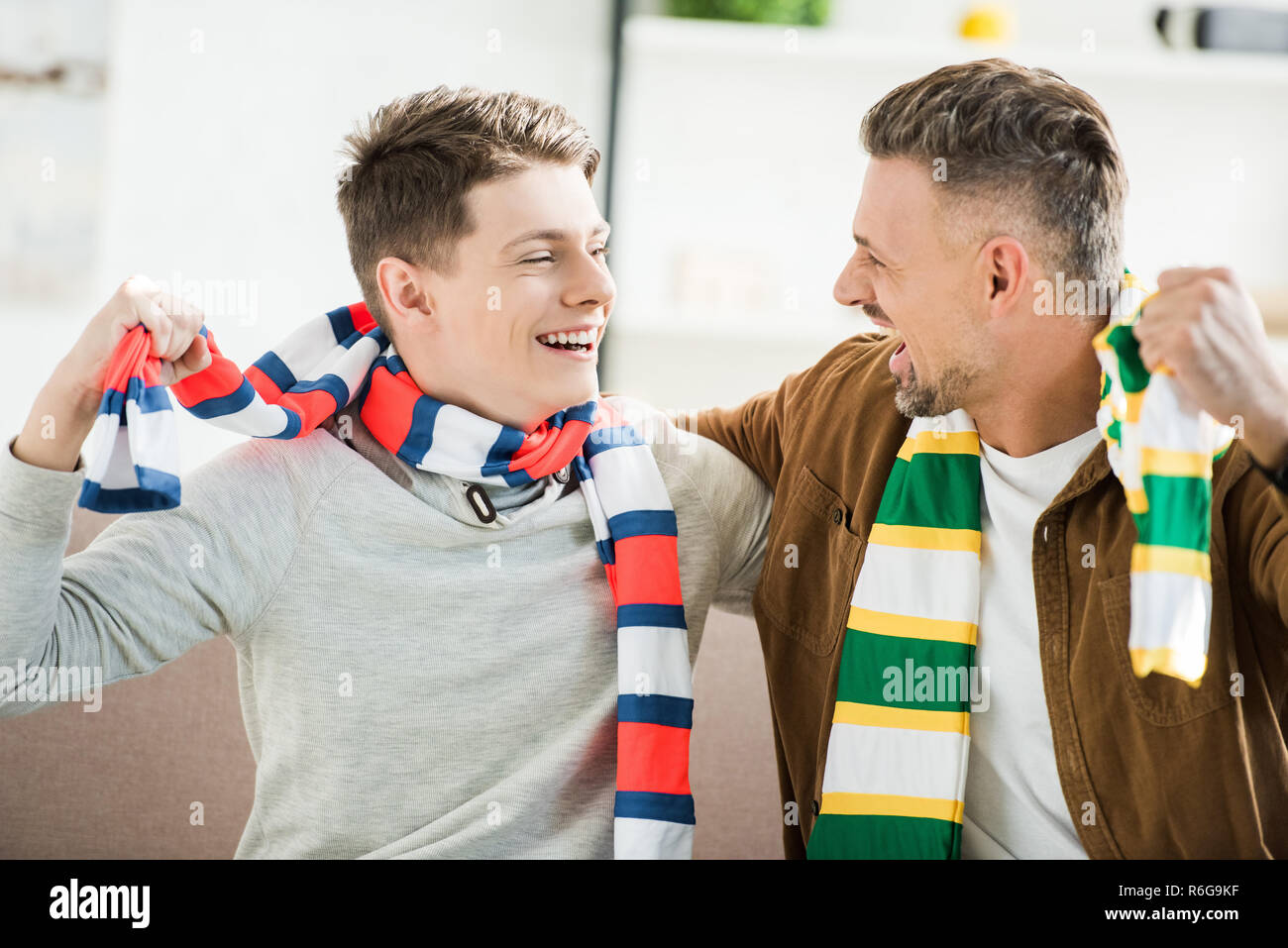 happy father and teen son in scarfs watching sport match at home ...