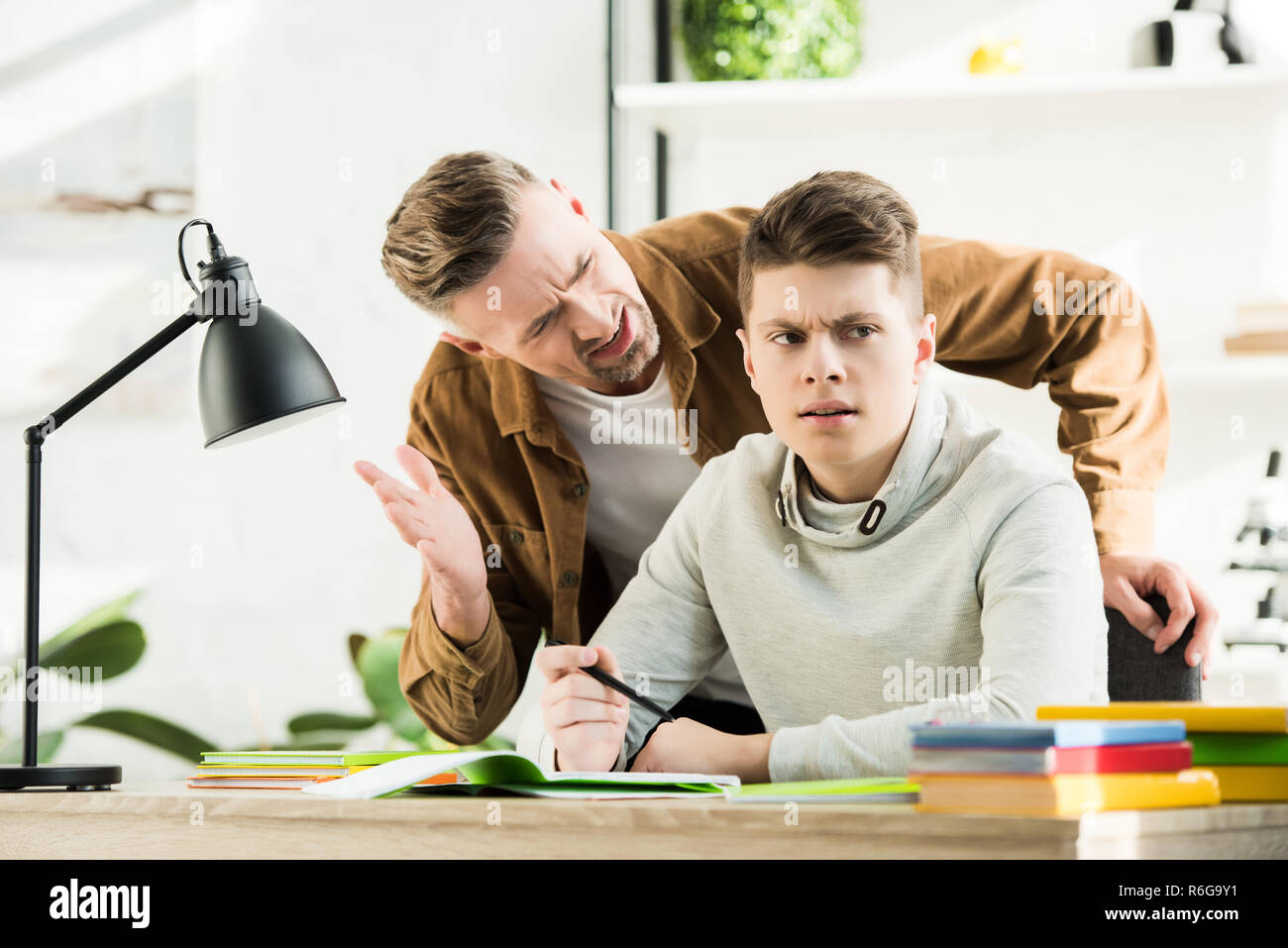 angry father gesturing and screaming at teen son, boy covering ears ...