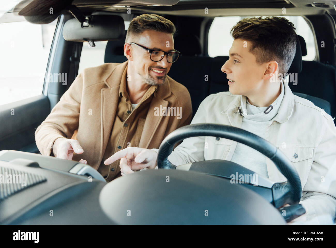 smiling handsome father teaching teen son driving car, they looking at ...