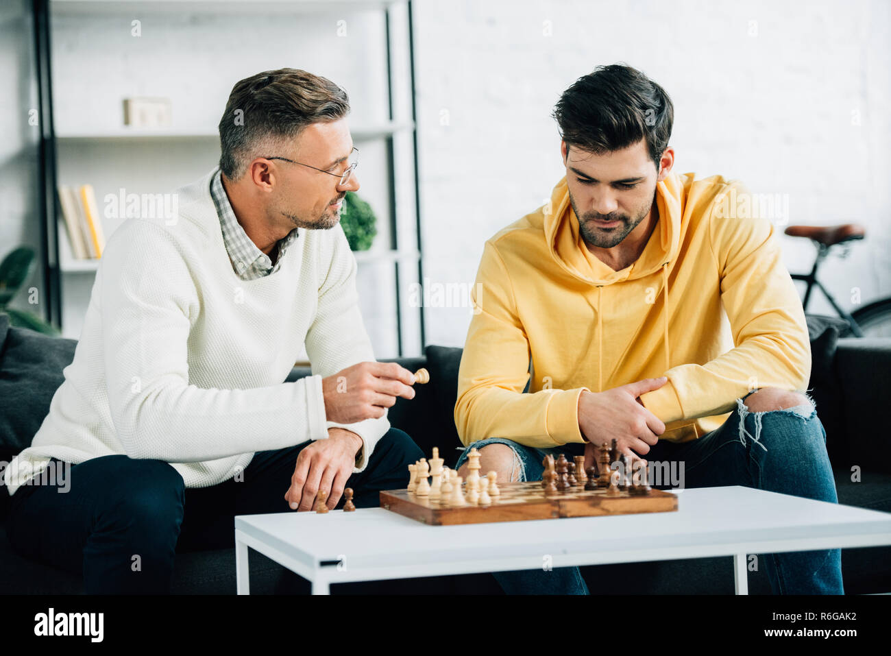 son and mature father playing chess together on weekend in living room ...