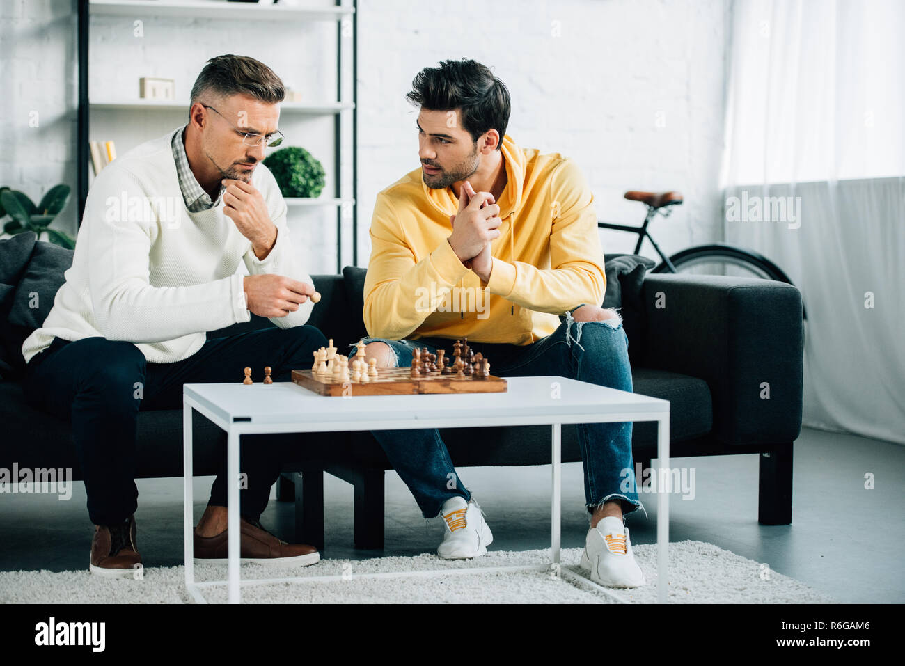 pensive son and mature father playing chess together on weekend at home ...
