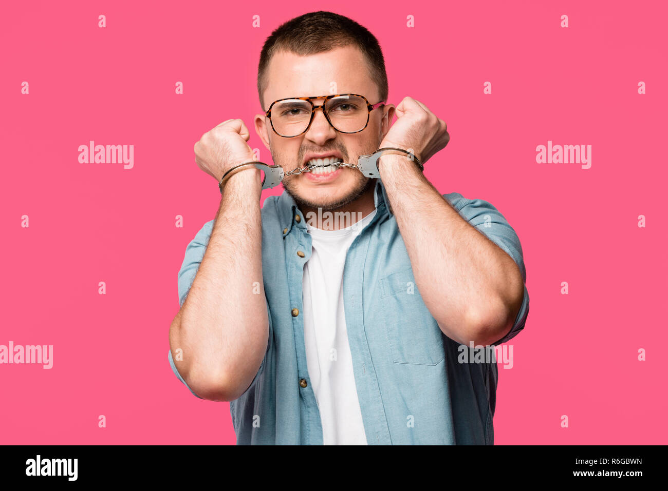 aggressive young man in eyeglasses biting handcuffs and looking at ...