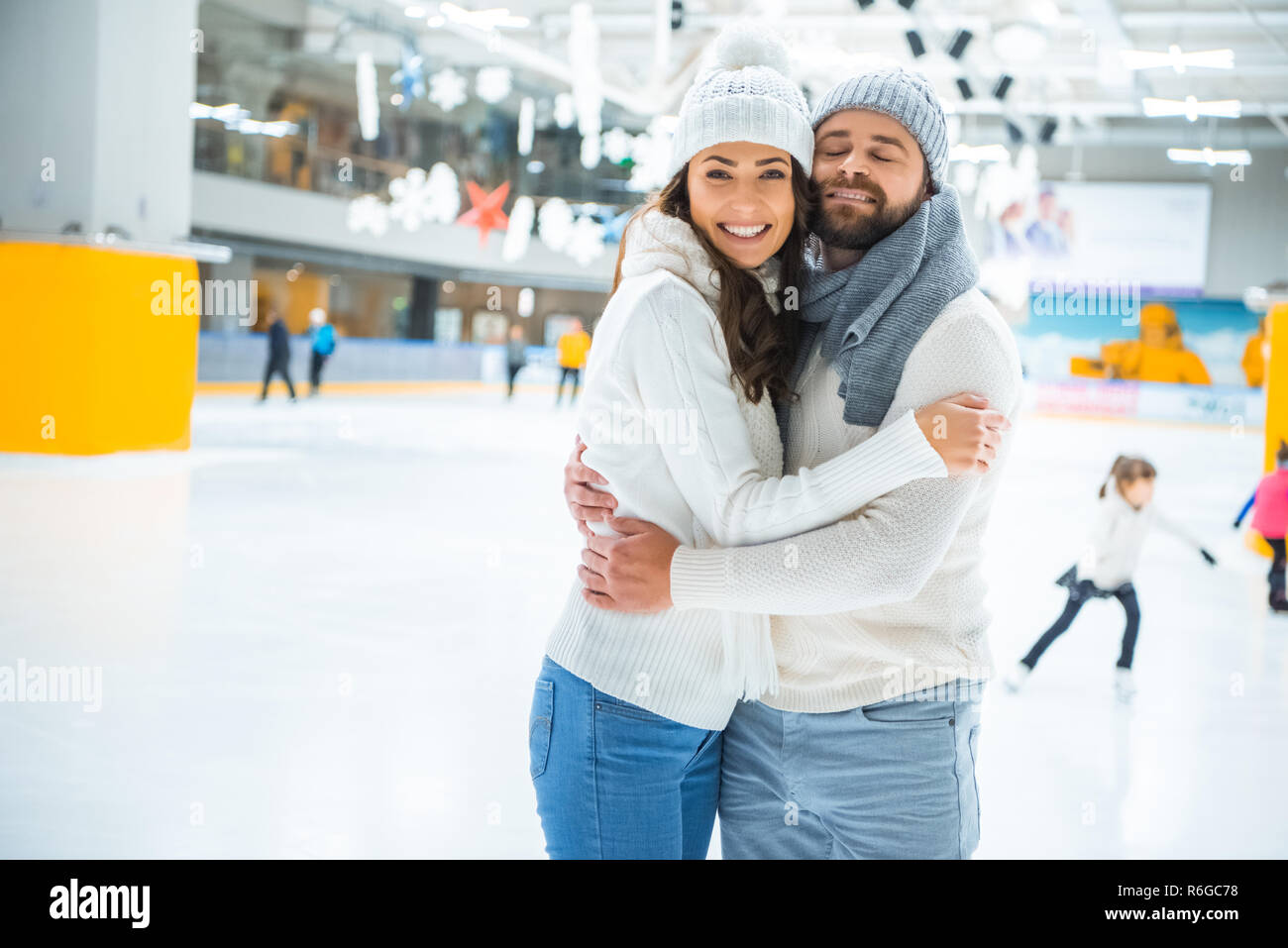 side view of couple in love hugging while skating on ice rink together ...