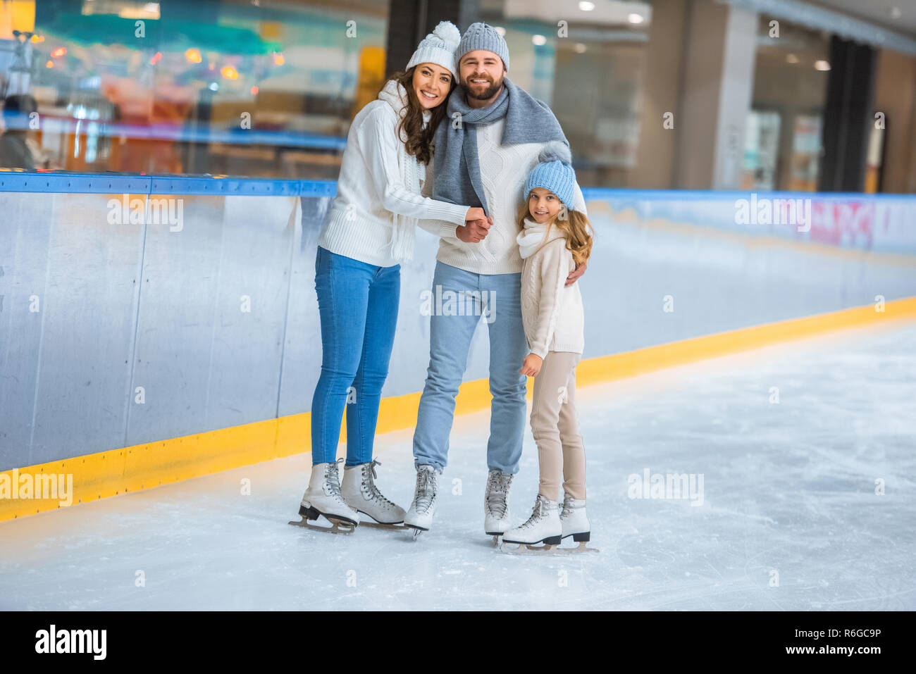 smiling parents and daughter in sweaters looking at camera on skating ...