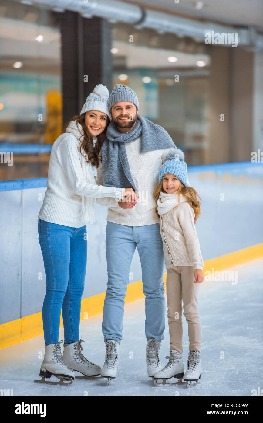 happy parents and daughter in sweaters looking at camera on skating ...