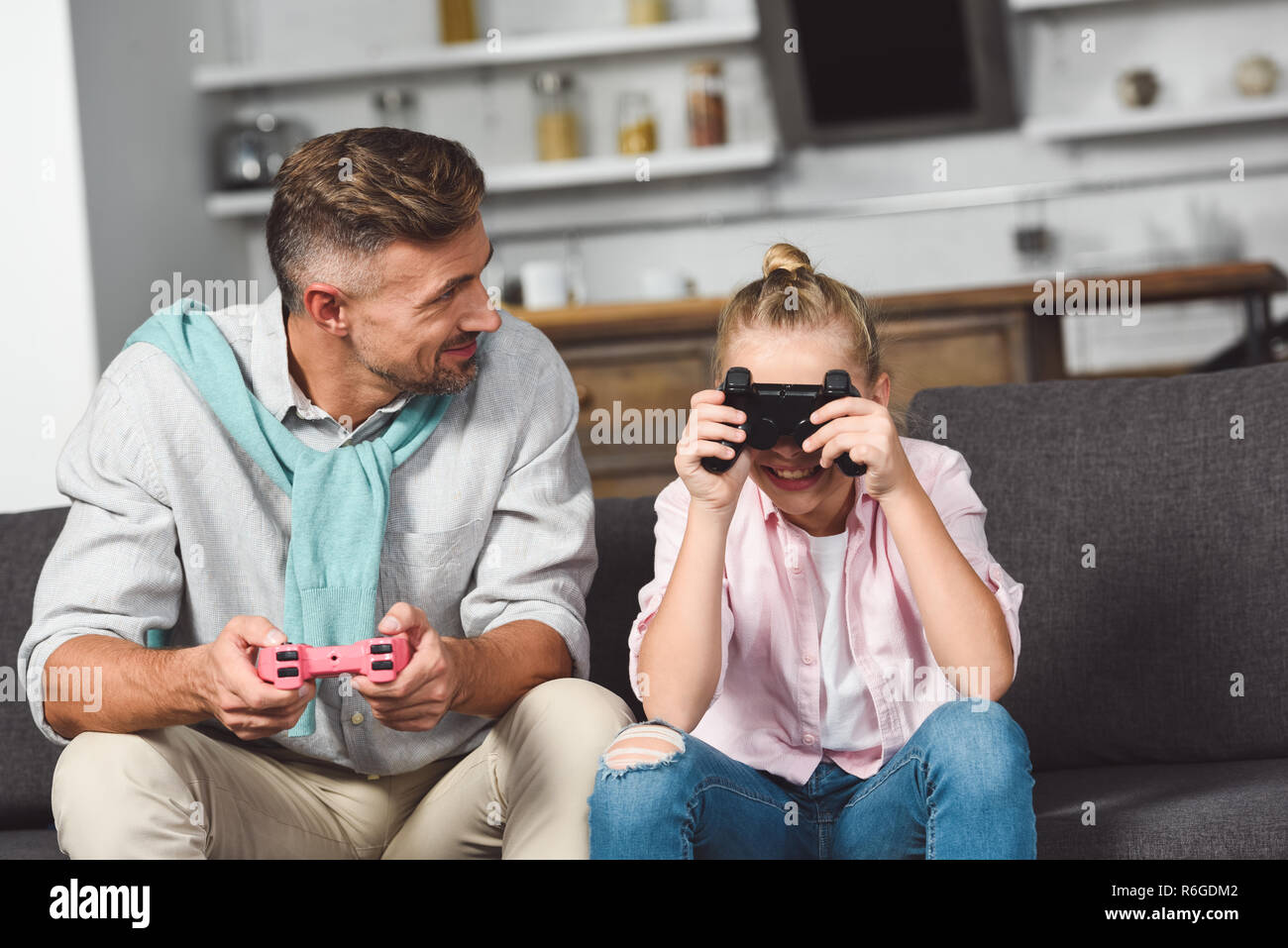 father looking at daughter while child hiding eyes behind joystick ...