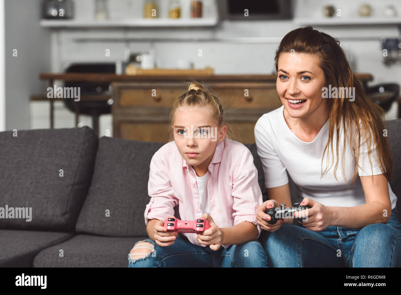 concentrated daughter playing video game with smiling mother Stock ...