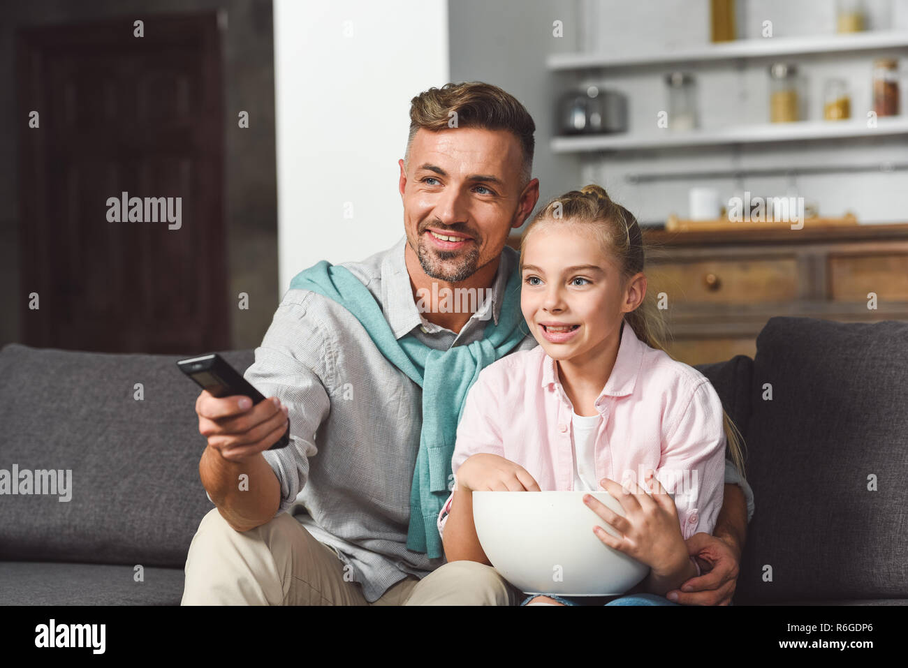 daughter eating popcorn from bowl while watching tv with father Stock ...