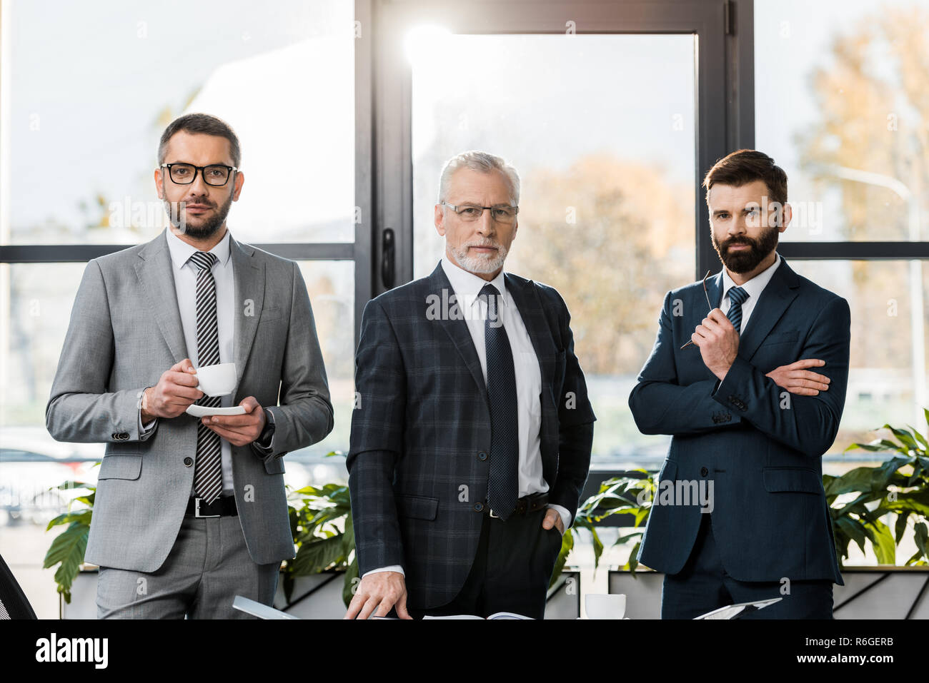 handsome businessmen in suits standing and looking at camera in office ...