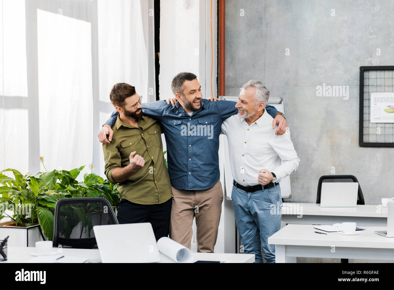 three smiling handsome businessmen hugging and standing in office Stock ...