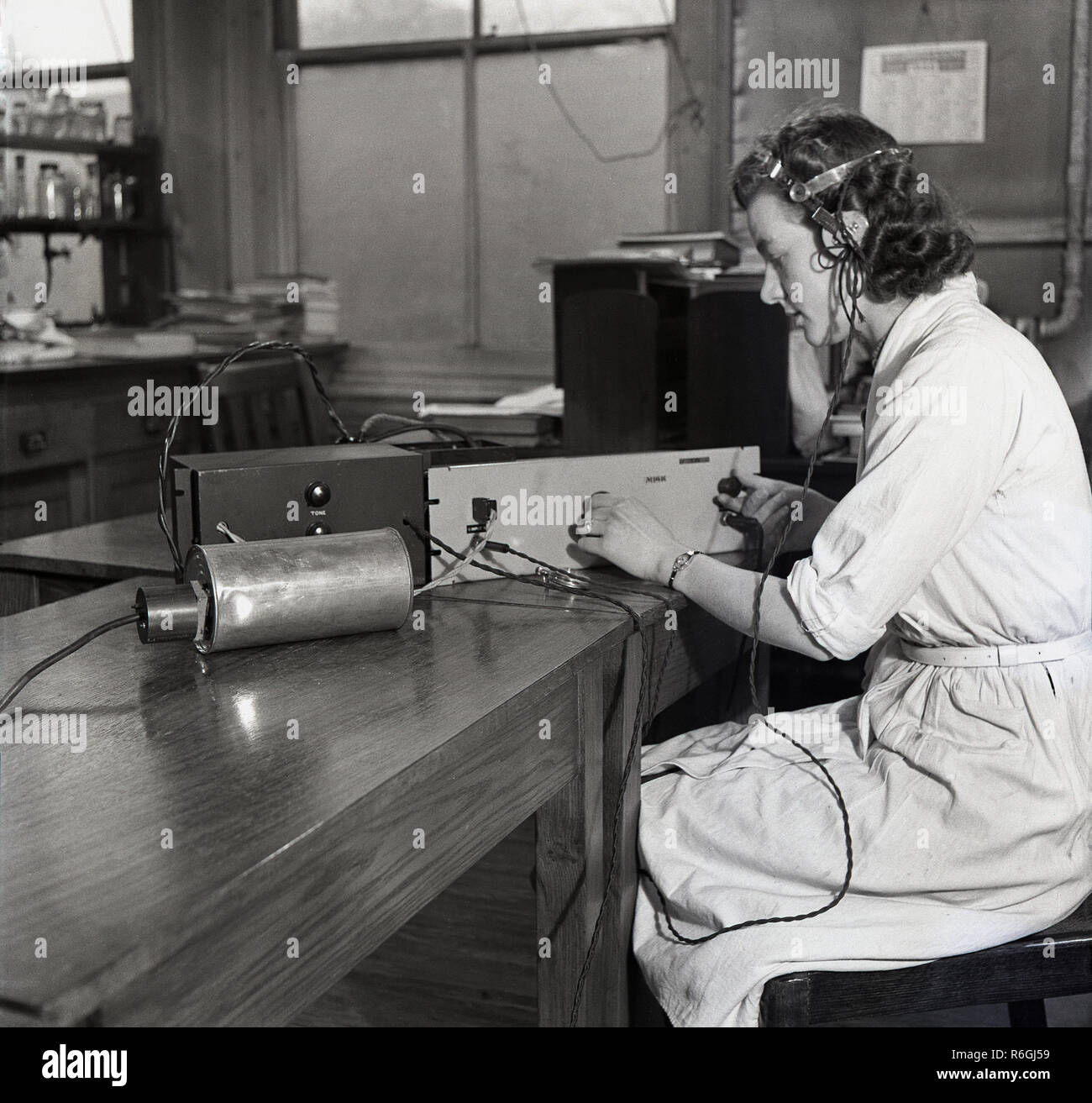 1950s, historical, a young lady sitting in a laboratory with headphones ...