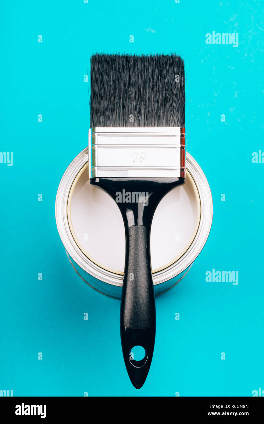 Brush with black handle on open can of white paint on blue background ...