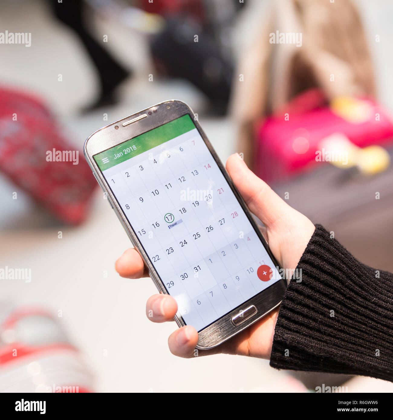 Woman checking calendar information on mobile phone sitting in airport ...