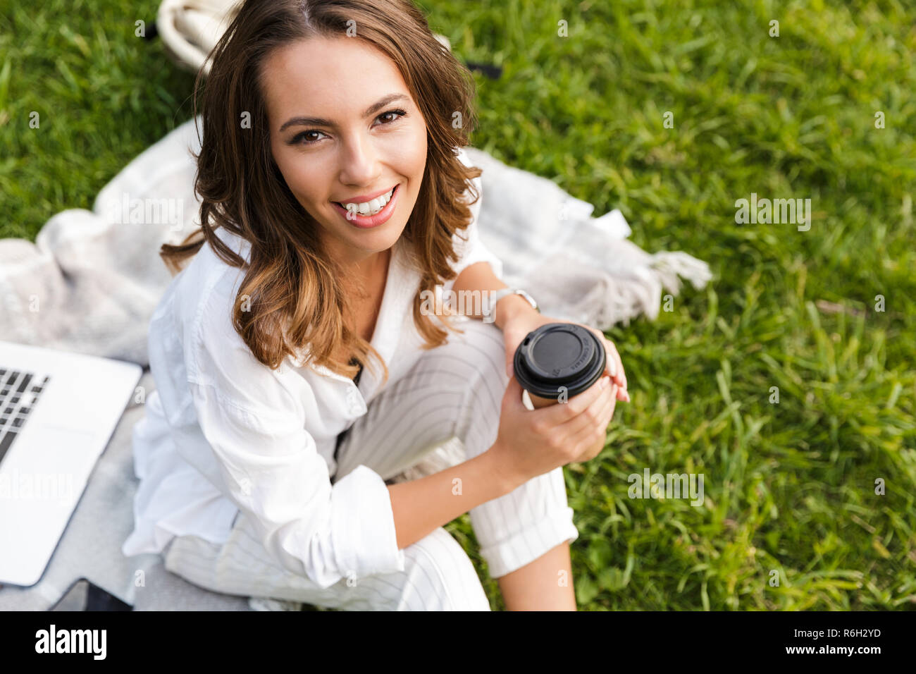 Smiling young woman spending time at the park, sitting on a grass with ...