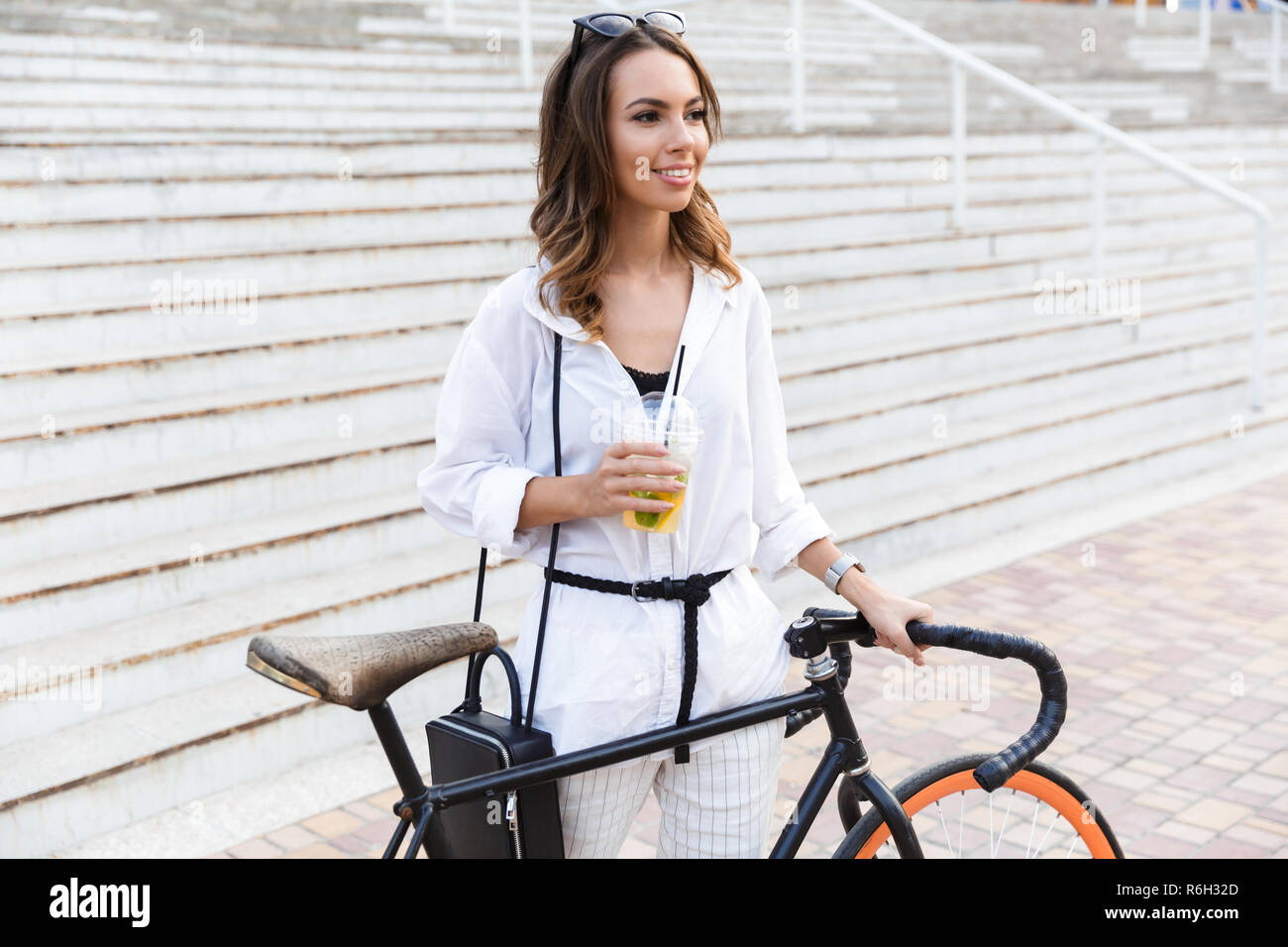 Happy young woman spending time at the park, walking with bicycle ...