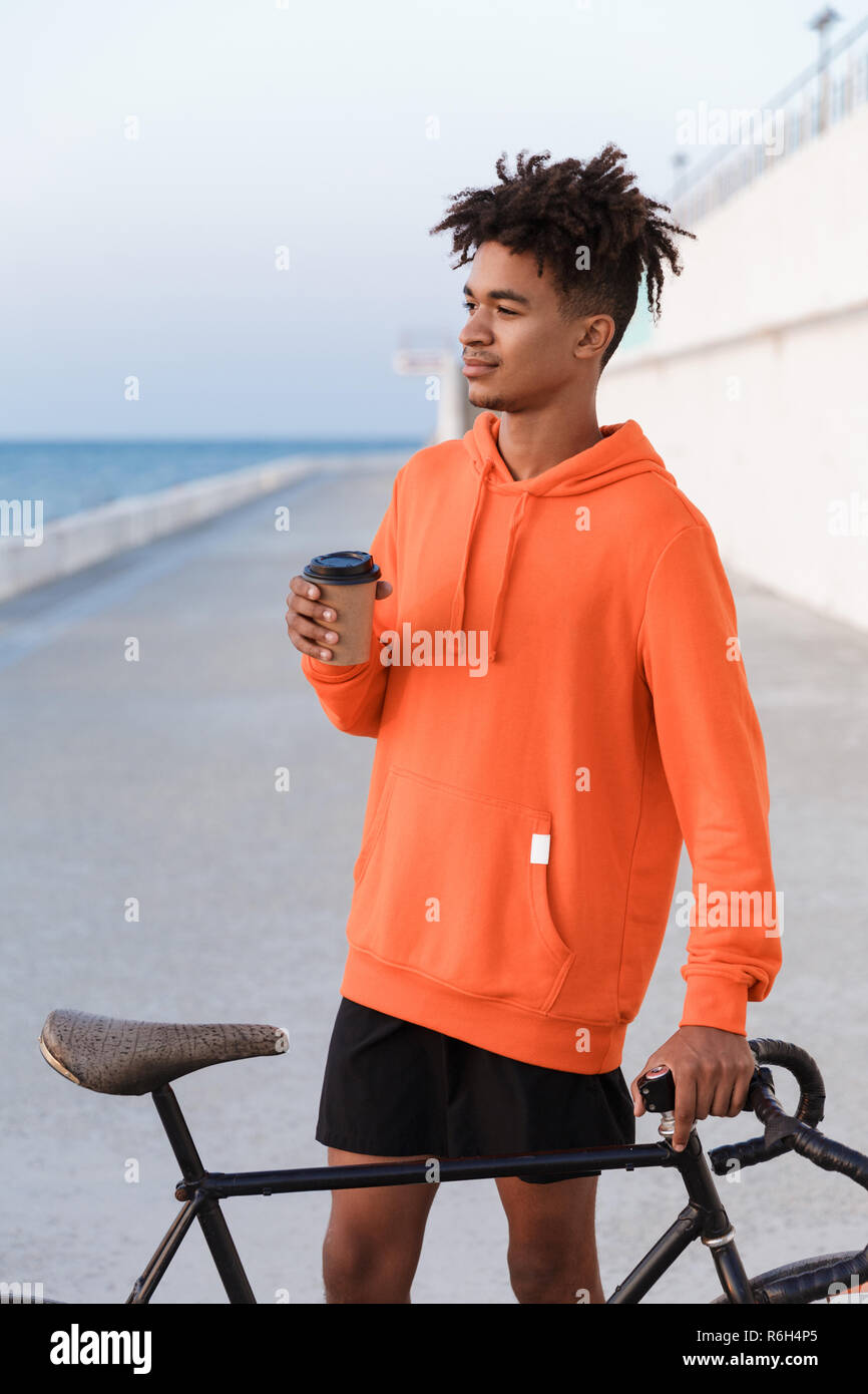 Image of a young sports guy outdoors on the beach with bicycle holding ...