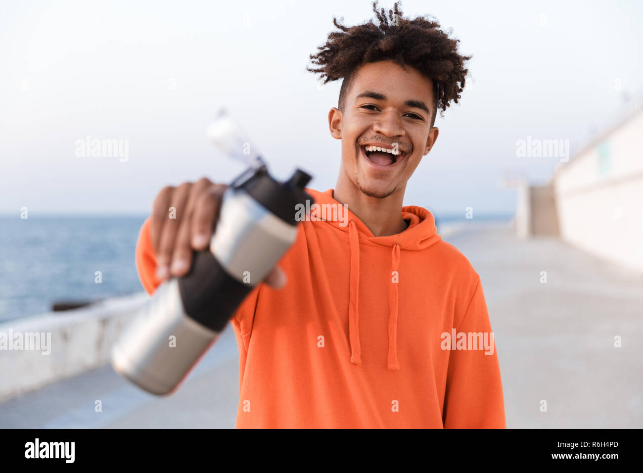 Image of a young sports guy outdoors on the beach drinking water ...