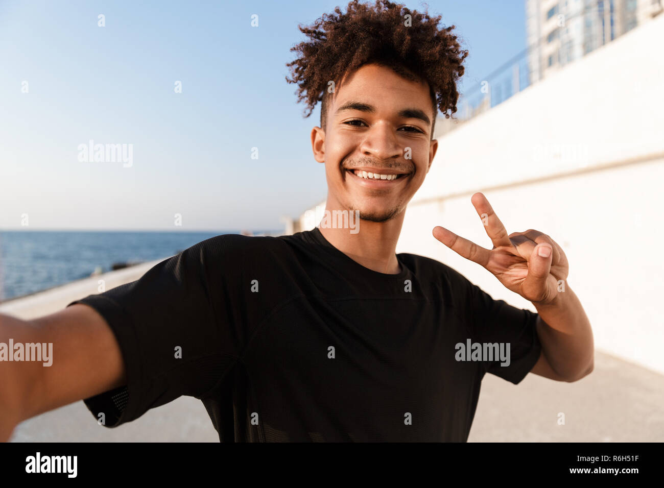 Smiling young african teenager sportsman standing at the beach, taking ...