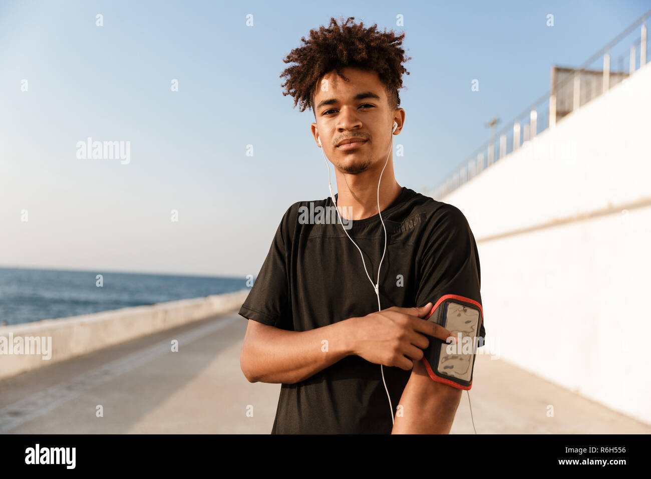 Smiling young african man dressed in sportswear standing at the beach ...