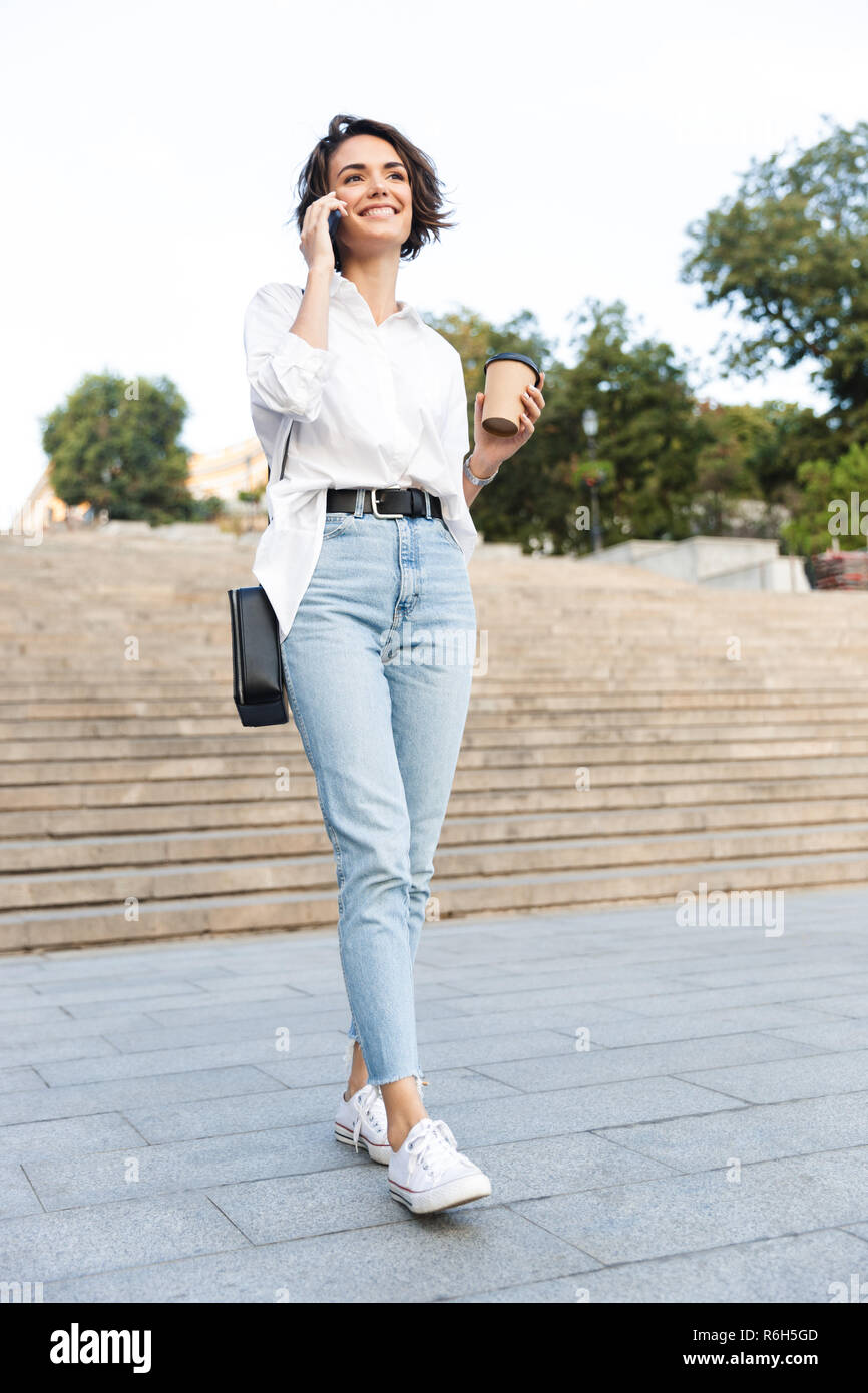Attractive young woman walking downstairs at the street, talking on ...