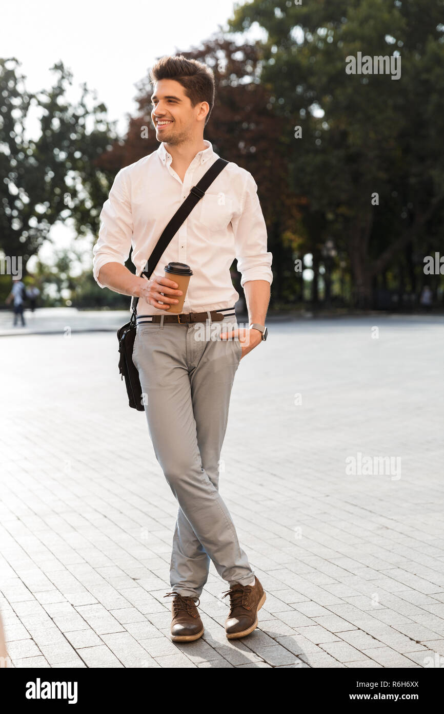 Full length photo of handsome man 30s wearing formal clothing drinking ...
