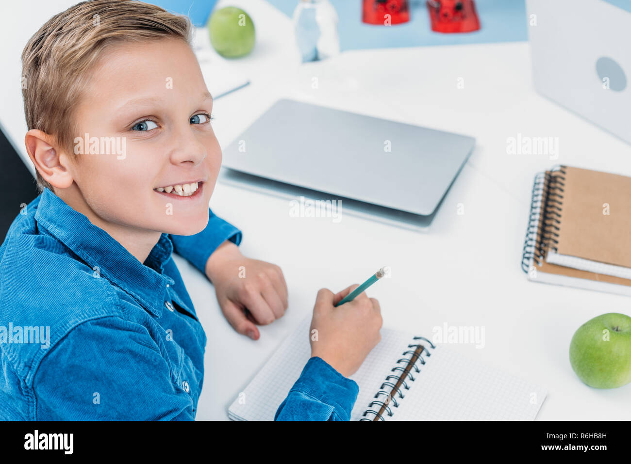smiling boy writing in notebook, smiling and looking at camera in stem ...