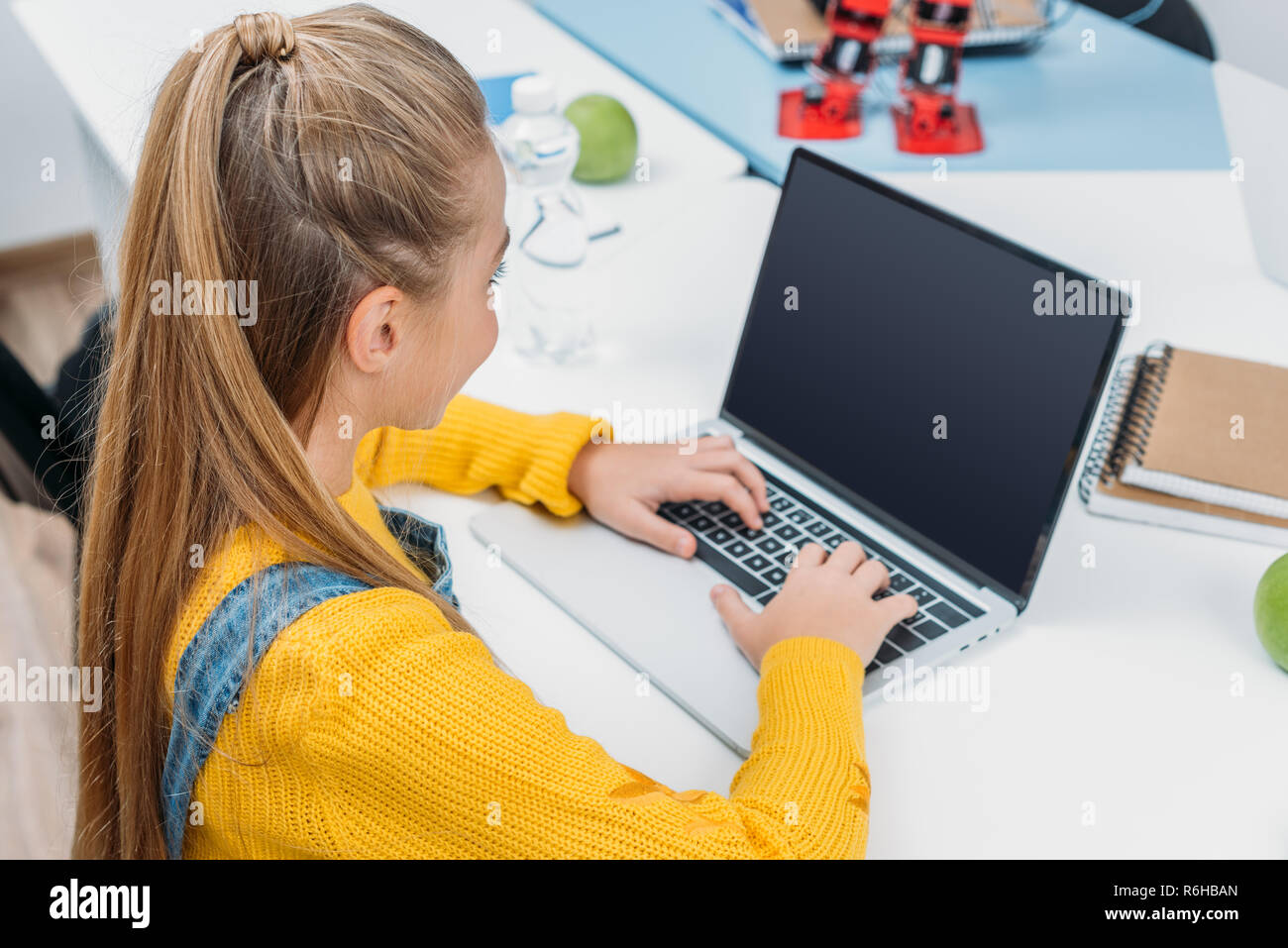 schoolgirl sitting at desk and typing on laptop keyboard during stem ...