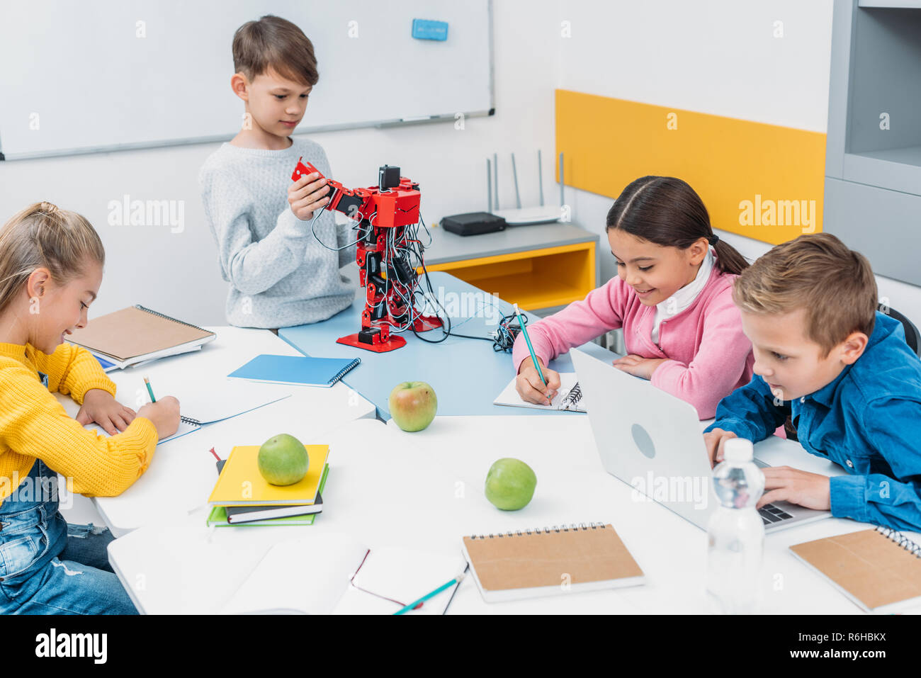 schoolchildren writing, using laptop, working on robot at STEM robotics ...