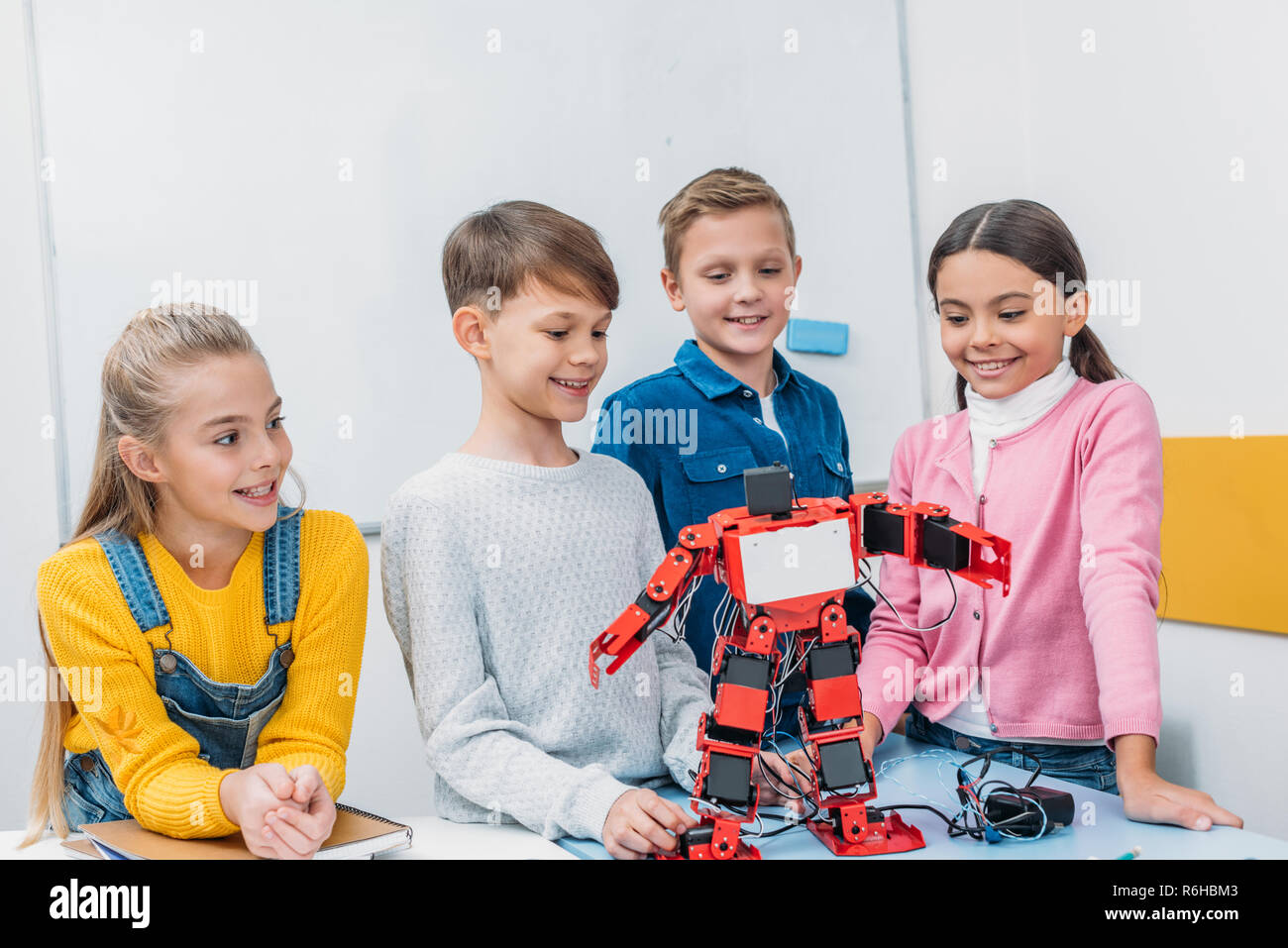 smiling schoolchildren looking at red robot handmade on desk in stem ...