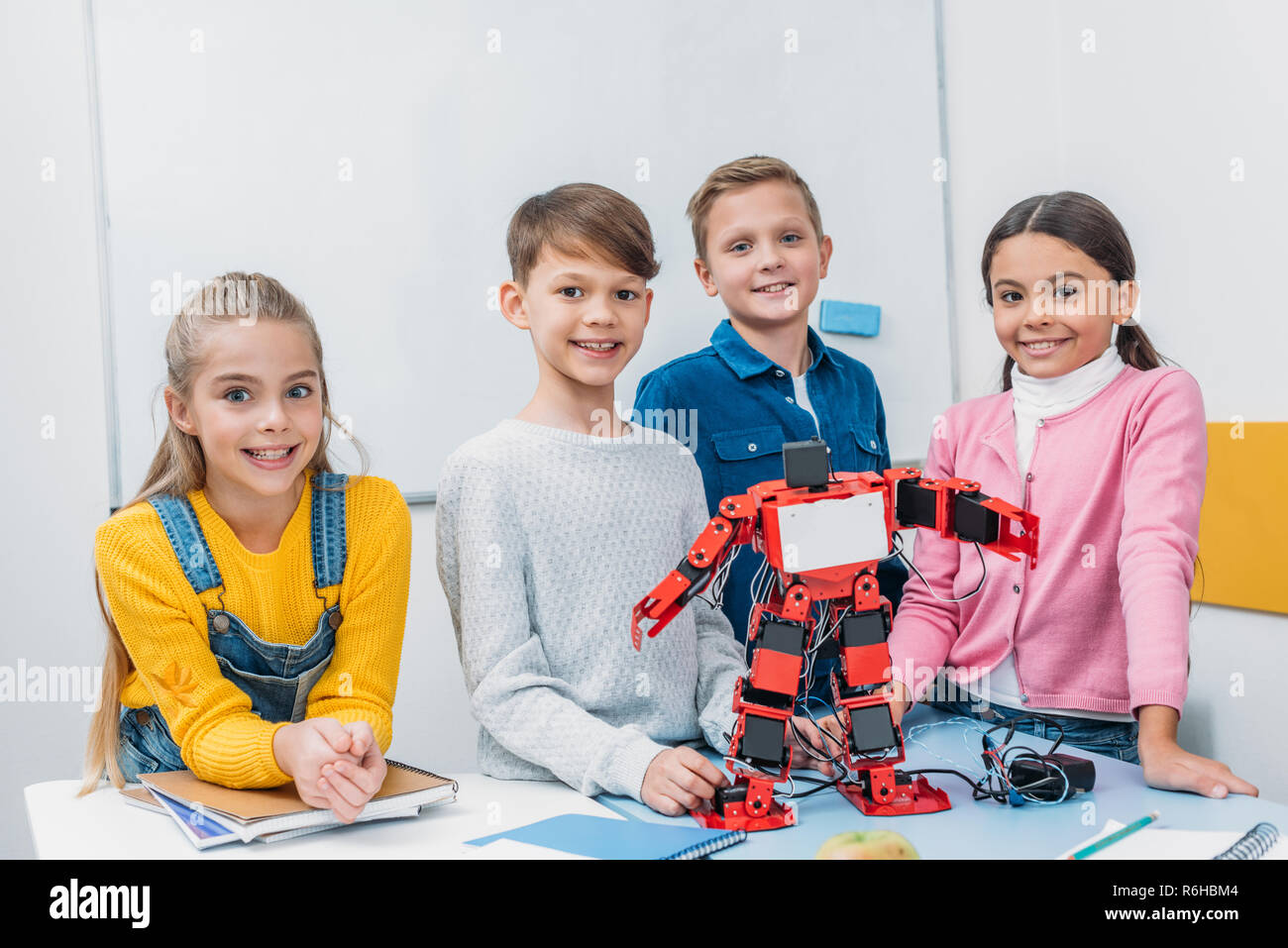 happy schoolchildren standing at desk with red electric robot in stem ...