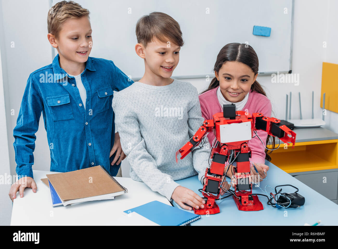 happy schoolchildren touching red handmade robot at desk in stem class ...