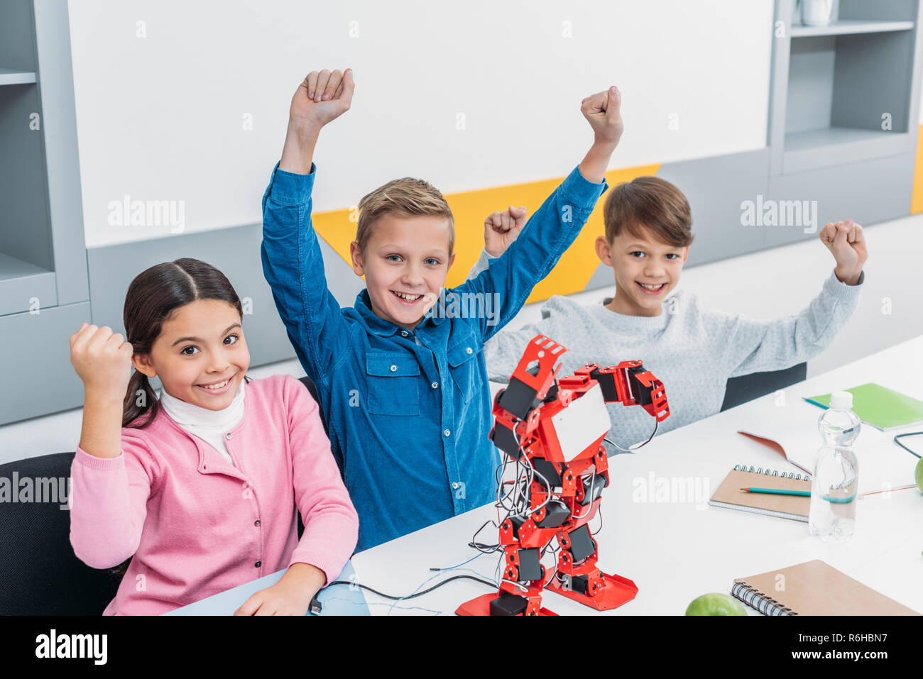 children joying and raising hands at desk with electric robot during ...