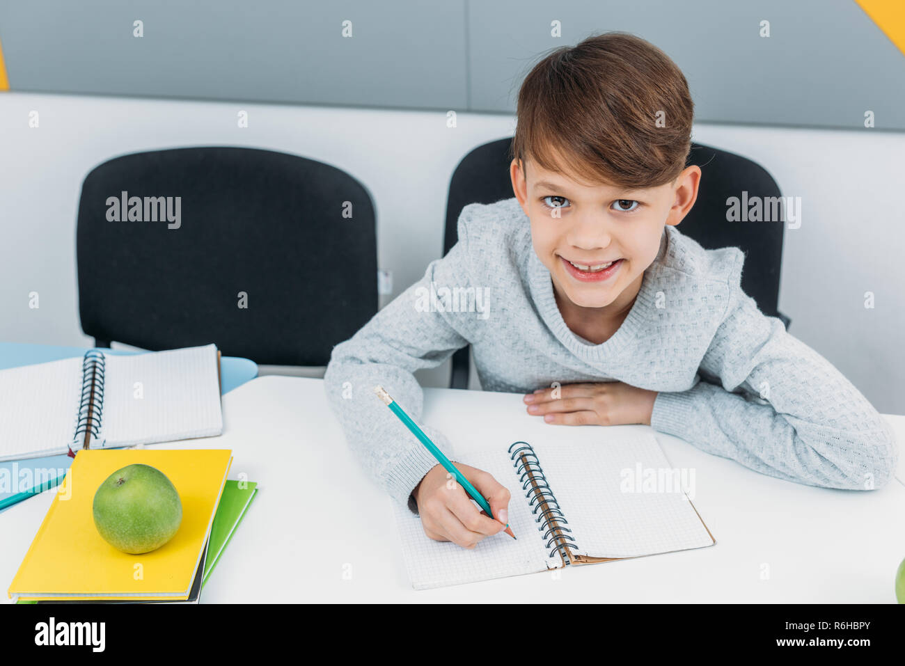 happy schoolboy writing in notepad in classroom Stock Photo - Alamy