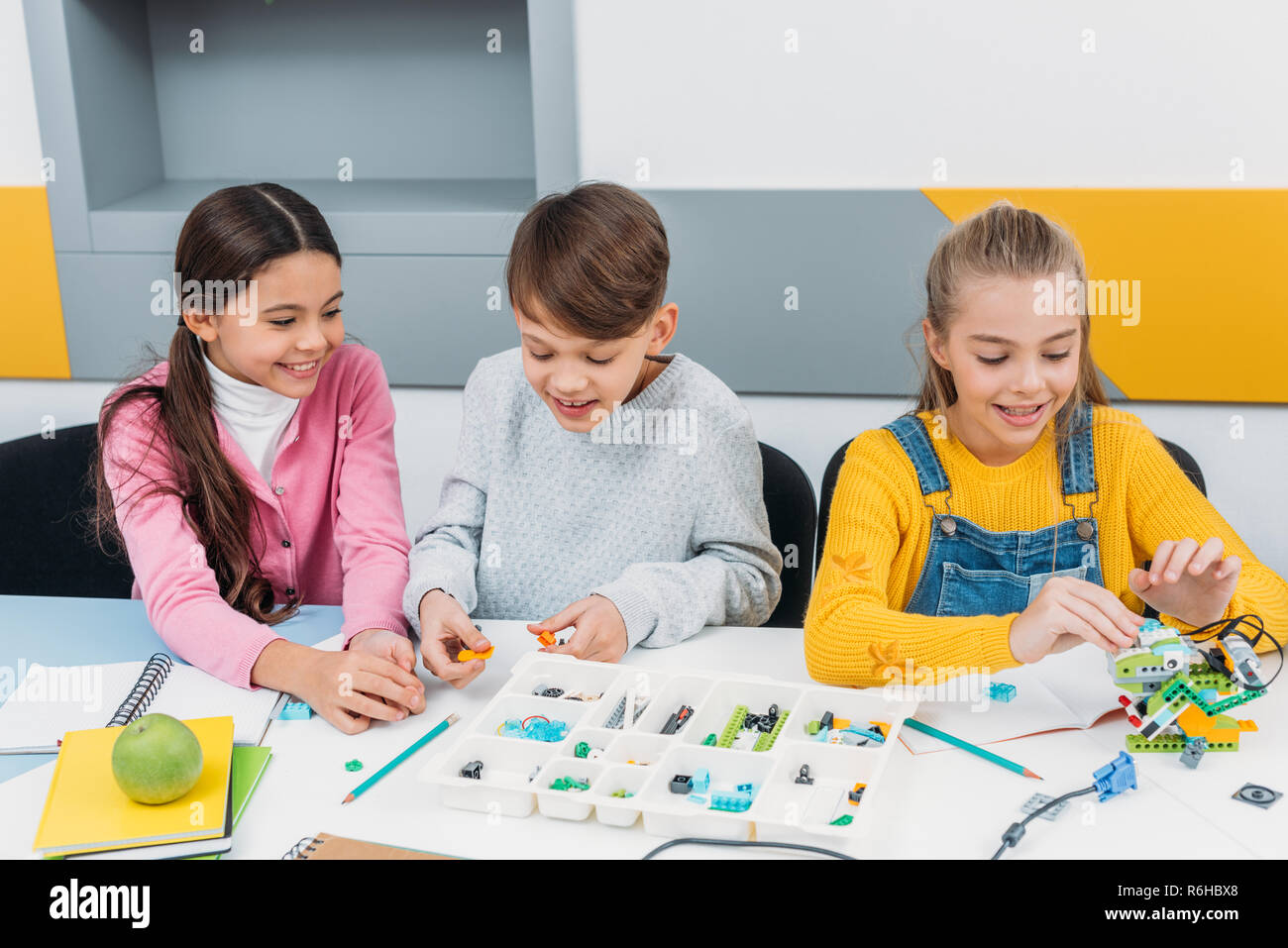 happy children sitting at desk and constructing robot in stem education ...