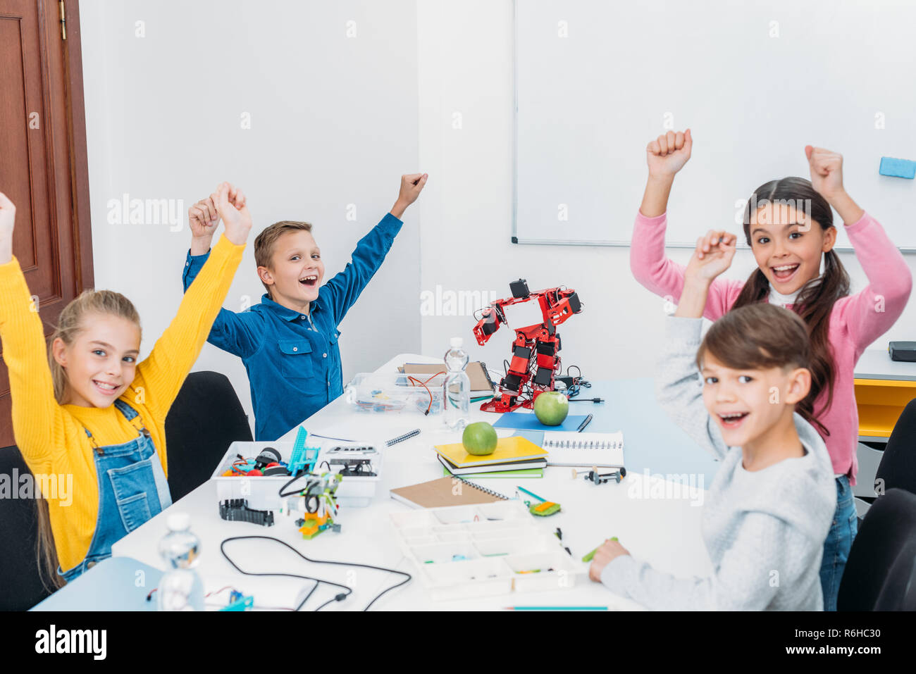 happy schoolchildren cheering and raising hands in air during STEM ...