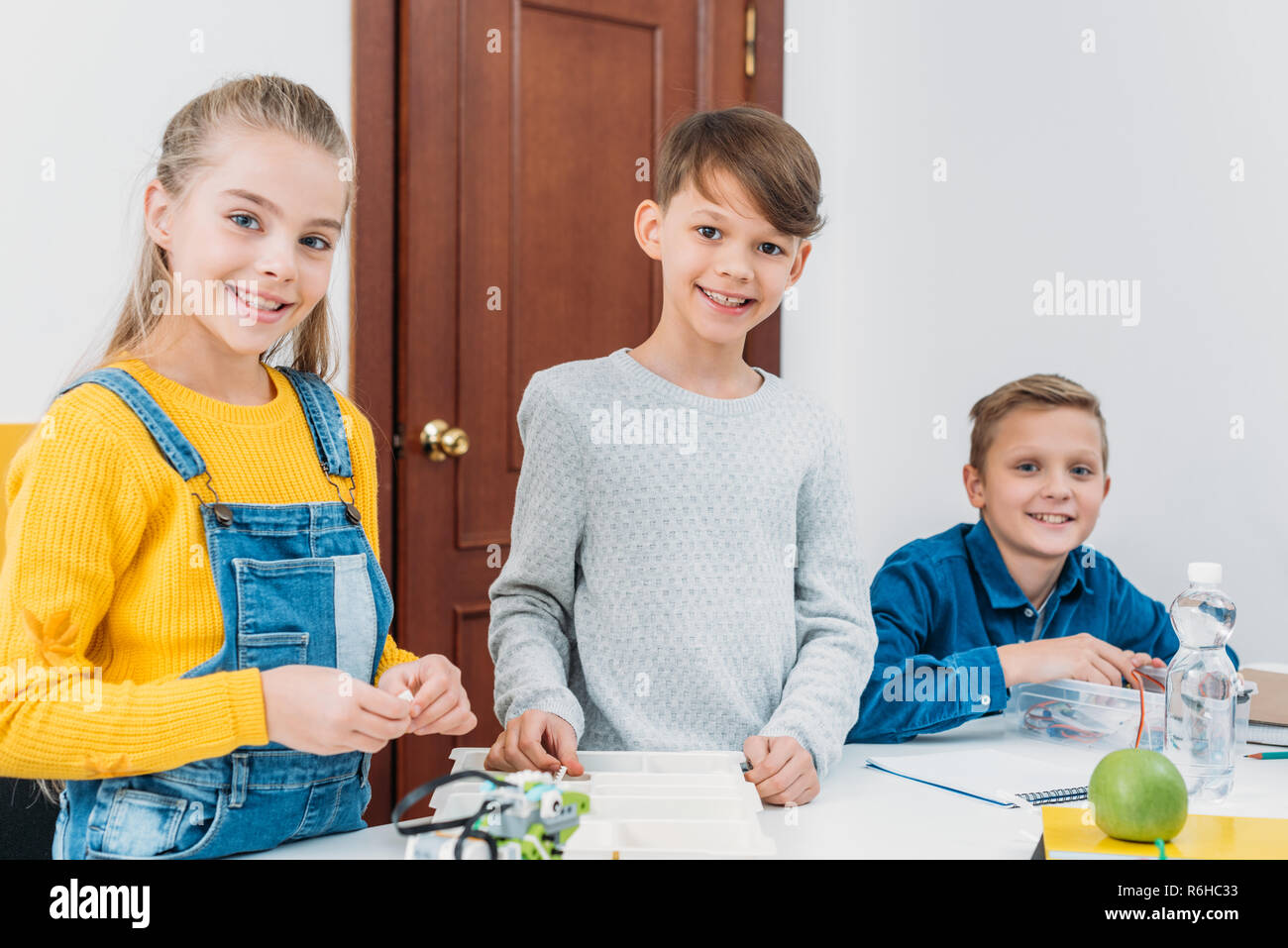 happy classmates at desk looking at camera and working in STEM ...