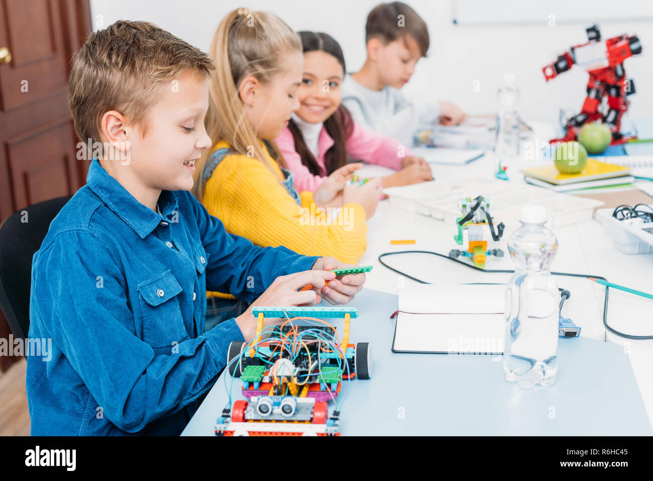 happy children sitting at desk and making robots in stem education ...