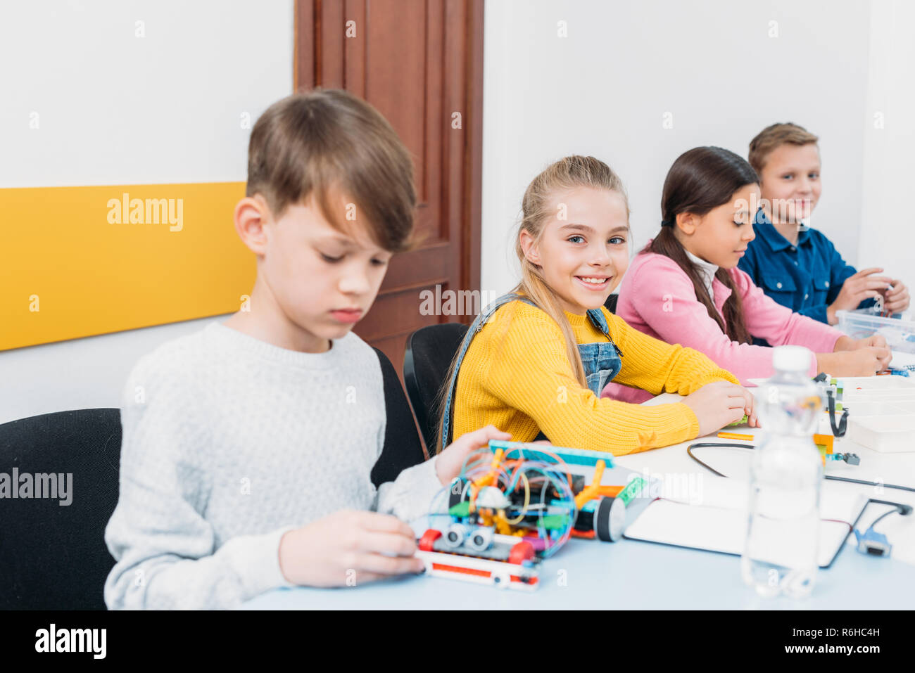 adorable schoolgirl looking at camera while classmates working at desk ...
