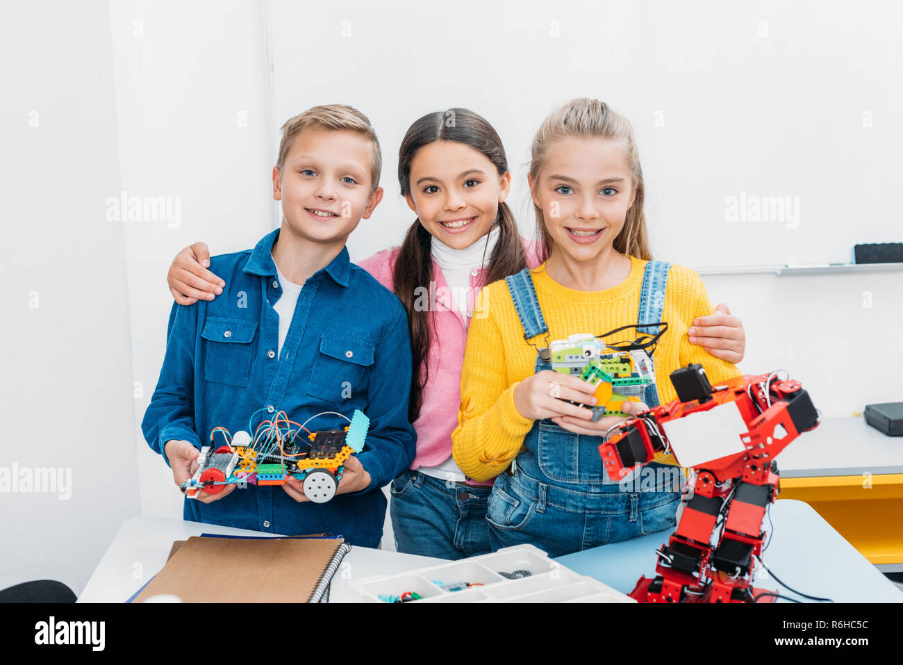 happy schoolchildren looking at camera and holding mechanical robots in ...