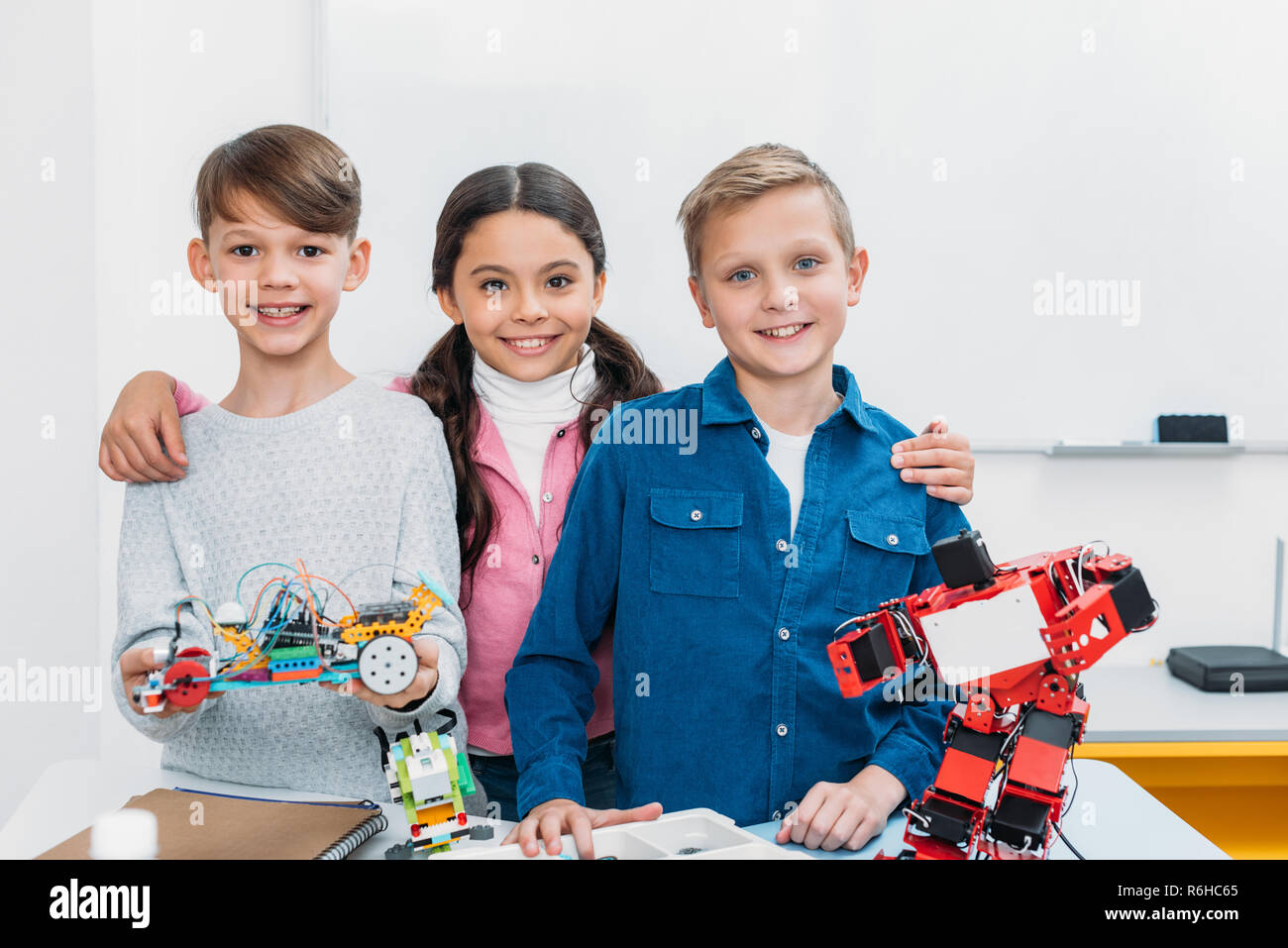 happy schoolchildren holding electric robot and looking at camera in ...