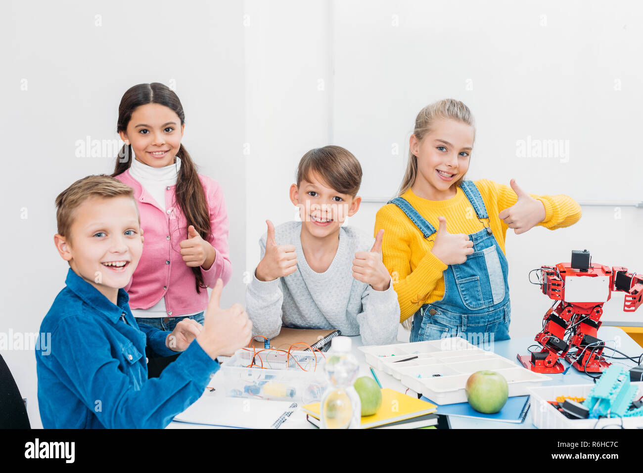 cheerful schoolchildren looking at camera and showing thumbs up while ...