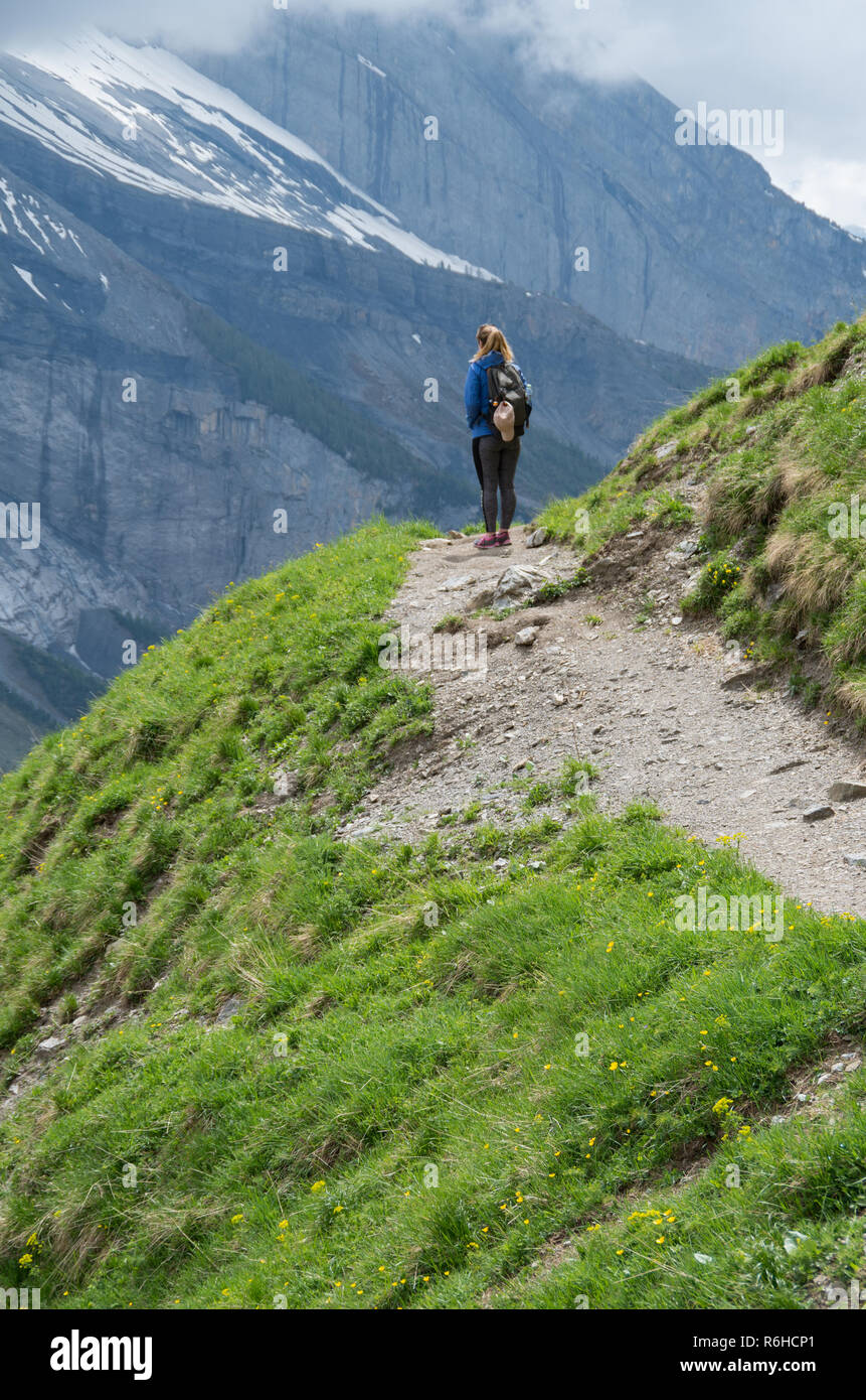 Young beautiful woman standing on a mountain path looking out over the ...