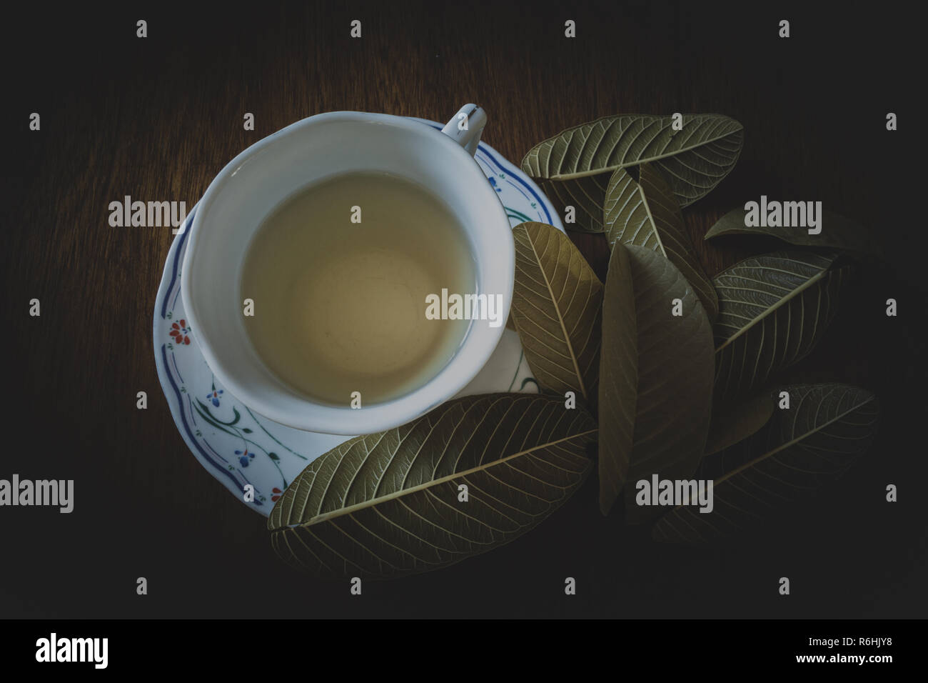 Common guava leaf tea. Cup, saucer and scattered boiled leaves on dark ...
