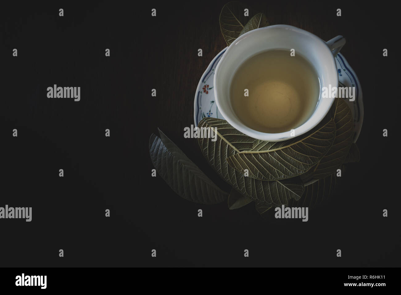 Common guava leaf tea. Cup, saucer and scattered boiled leaves on dark ...