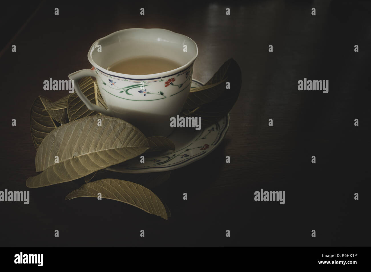 Common guava leaf tea. Cup, saucer and scattered boiled leaves on dark ...