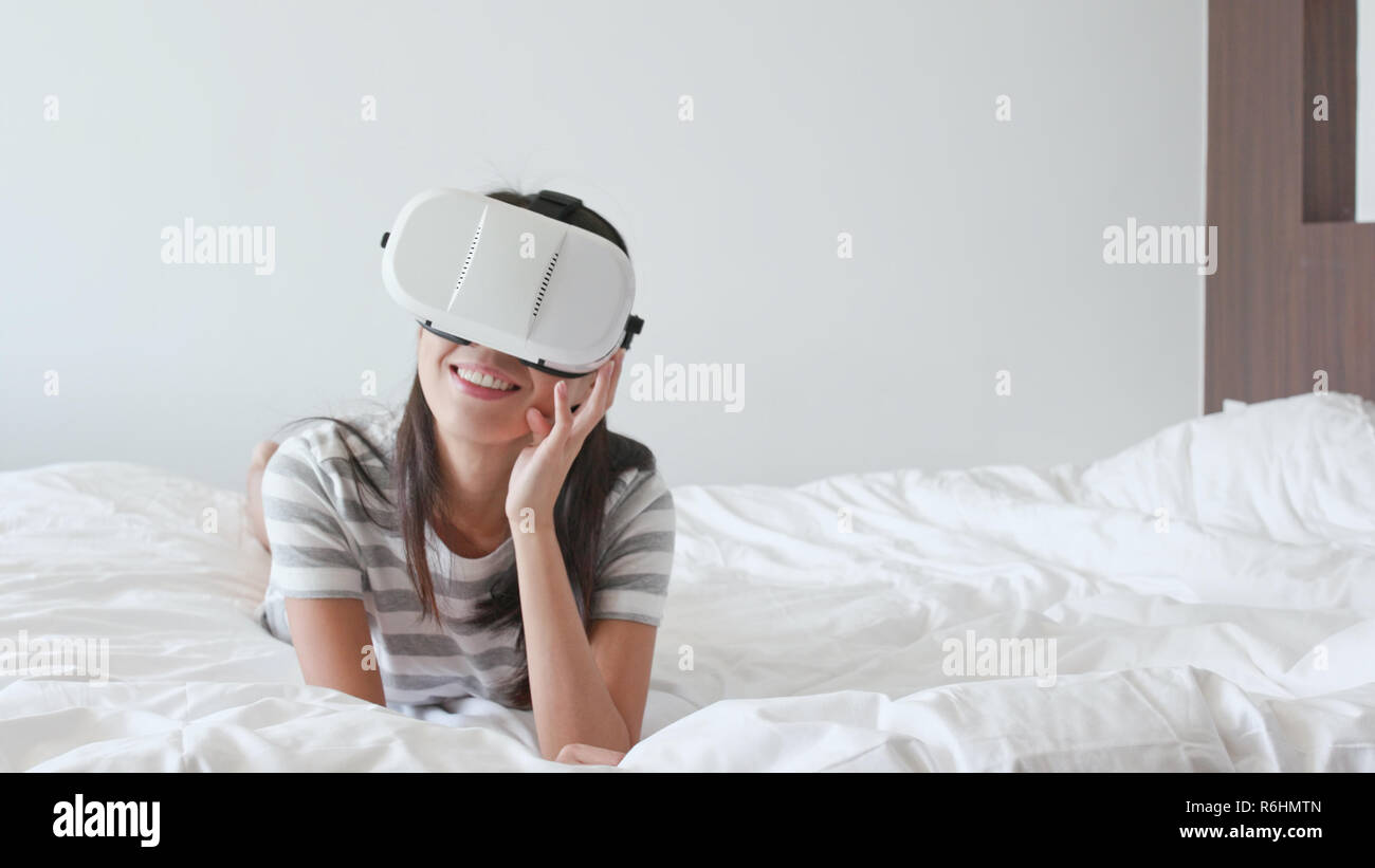 Woman looking though virtual reality device and lying on bed Stock ...