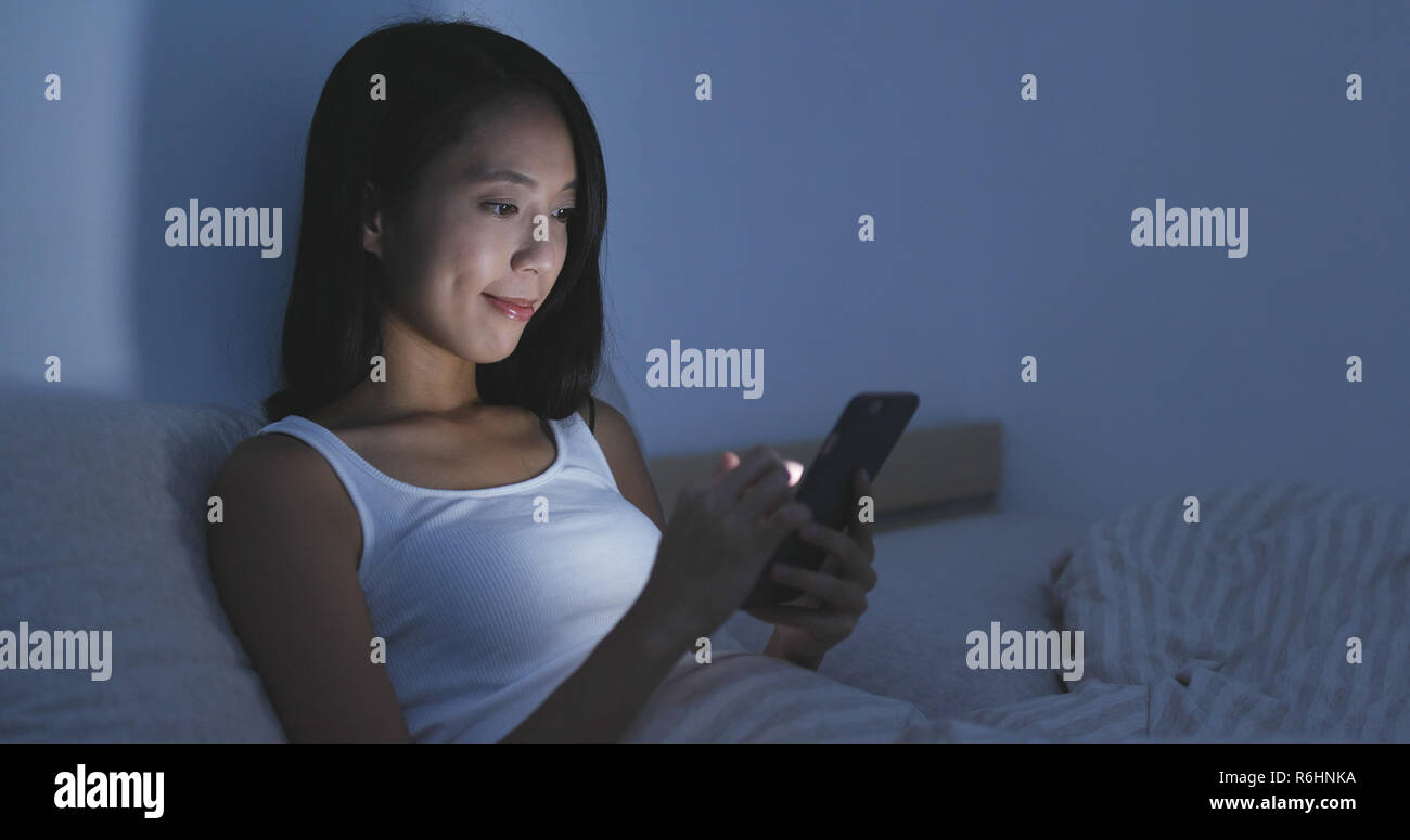 Woman looking at cellphone on bed Stock Photo - Alamy