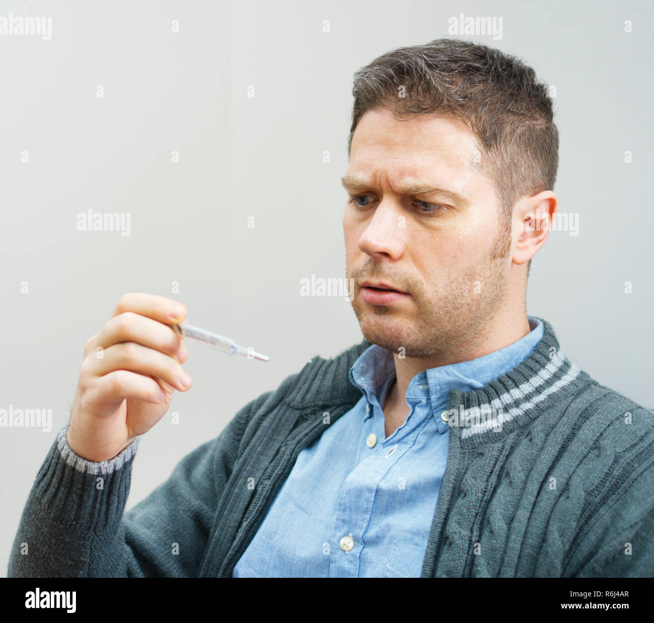 Sad handsome man looking at thermometer Stock Photo - Alamy