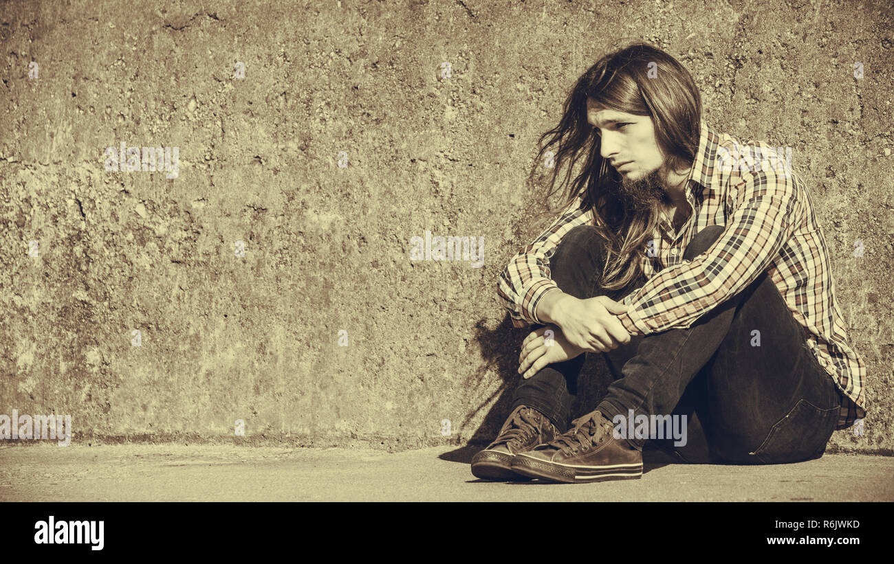 Man bearded long hair sitting sad alone by grunge wall outdoor ...